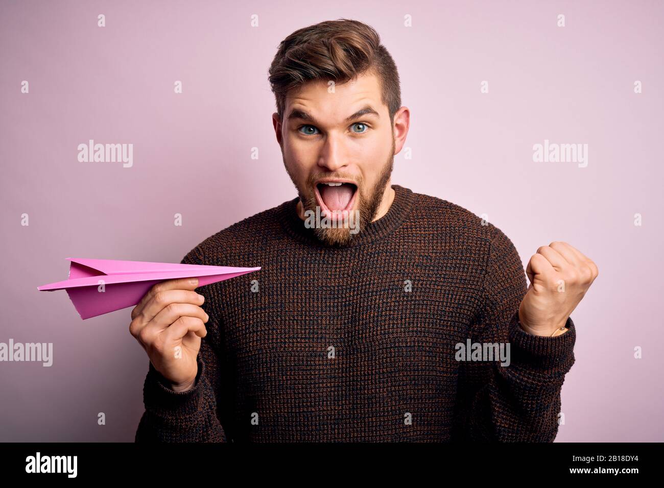 Young blond man with beard and blue eyes holding pink paper plane over ...