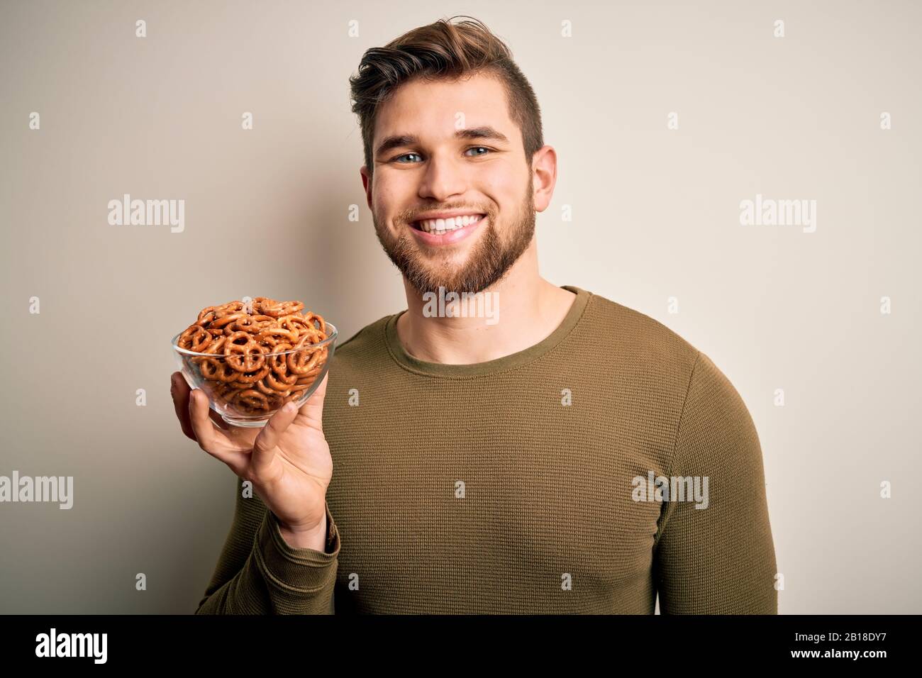 Young blond German man with beard and blue eyes holding bowl with baked ...