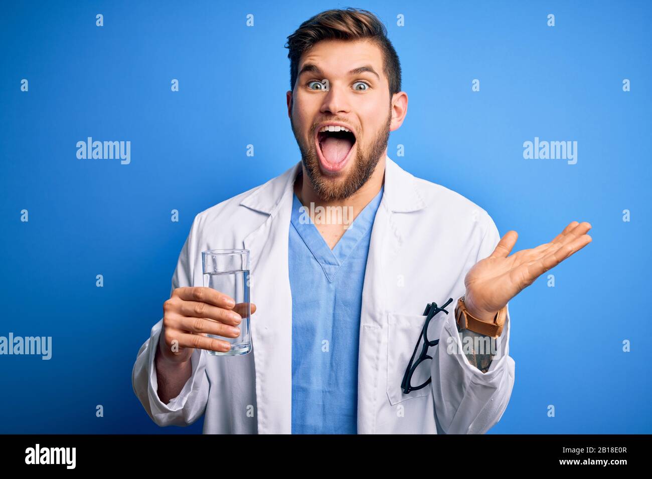 Young blond doctor man with beard and blue eyes wearing coat drinking ...