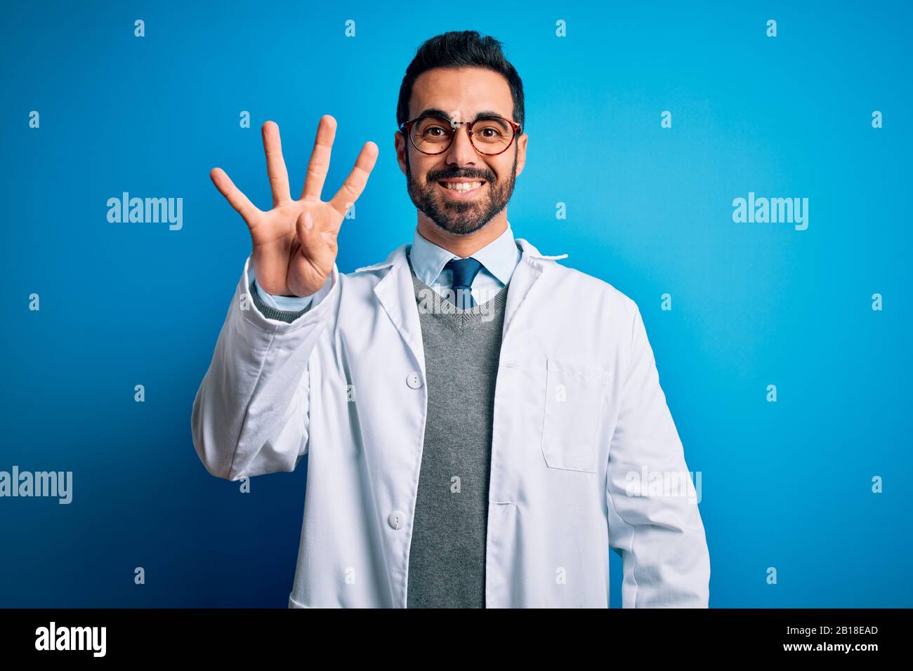 Young Handsome Doctor Man With Beard Wearing Coat And Glasses Over Blue