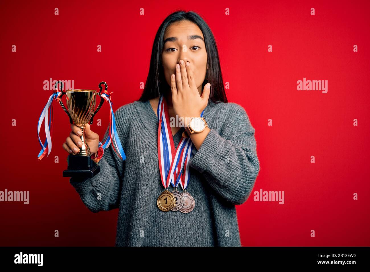 Young beautiful champion asian woman holding trophy wearing medals over ...