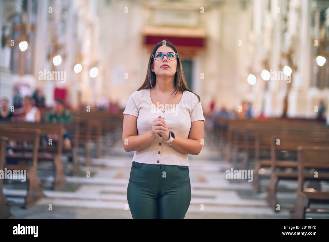 Young beautiful woman standing with hands together praying at church ...