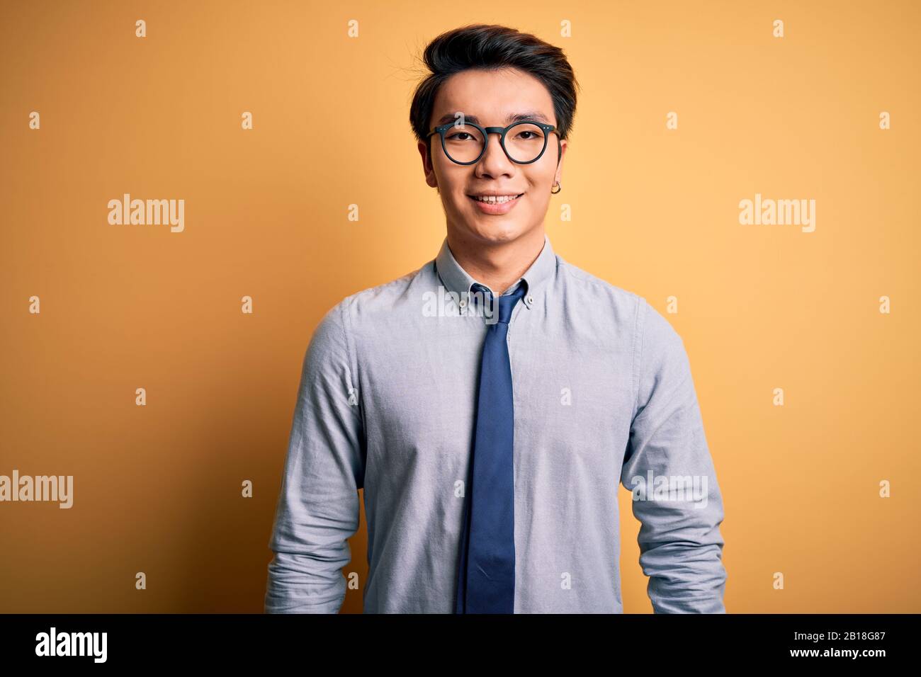 Young handsome chinese businessman wearing glasses and tie over yellow ...