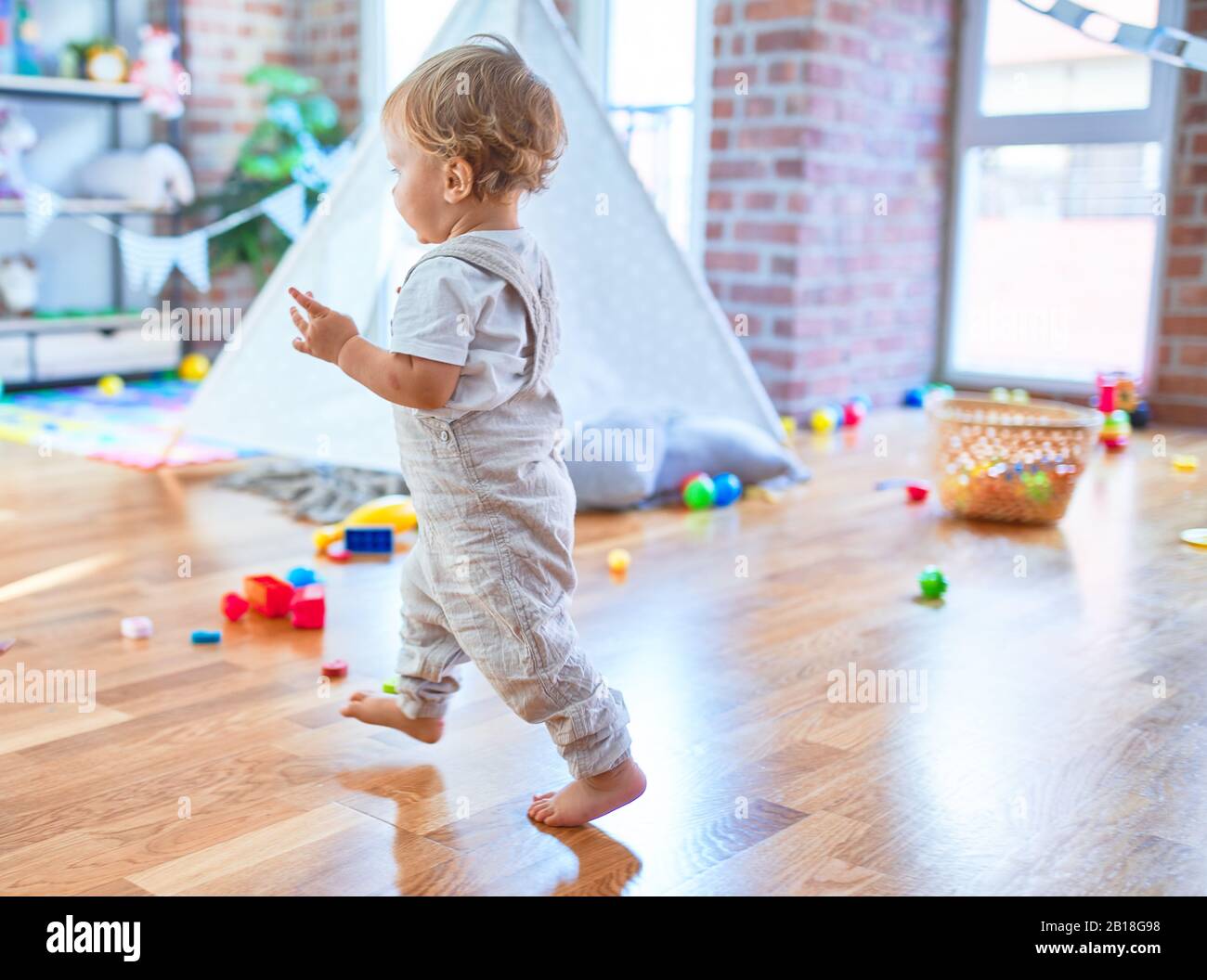 Adorable blonde toddler playing around lots of toys at kindergarten ...