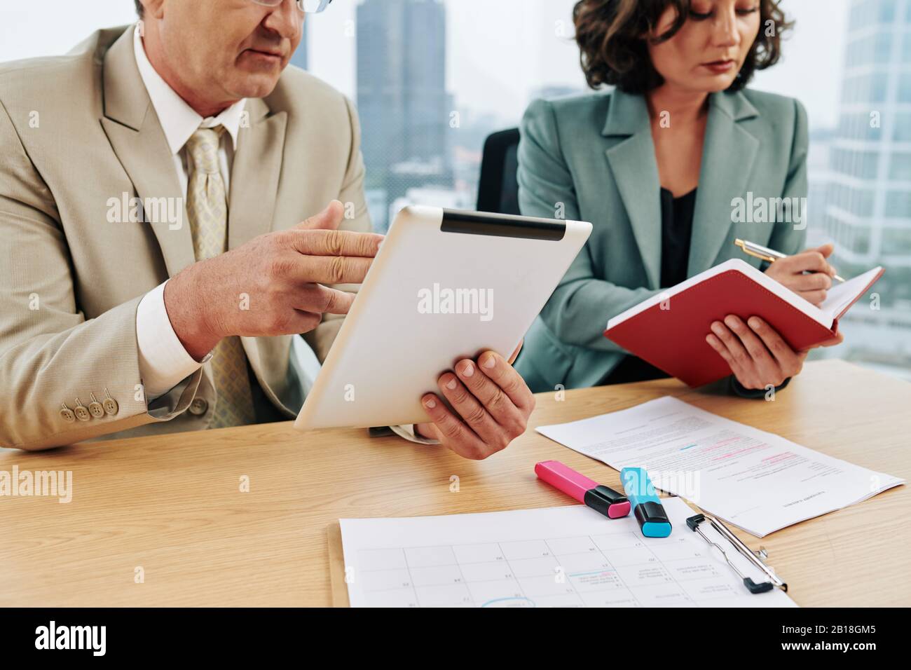 Businessman reading report on talet computer when his colleague writing ...