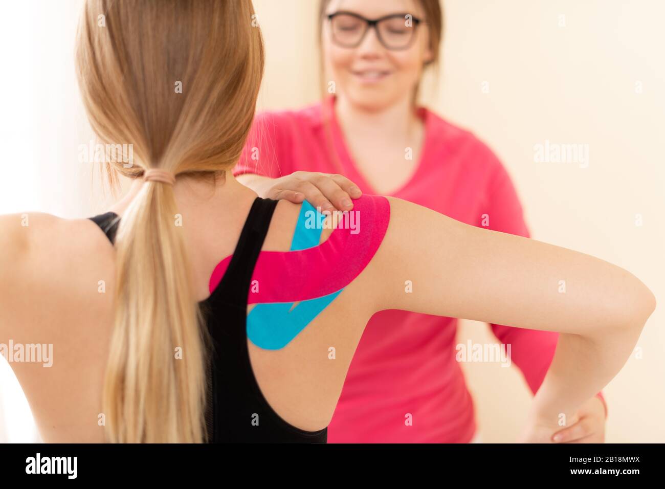 Young female patient wearing kinesio tape on her shoulder exercising ...
