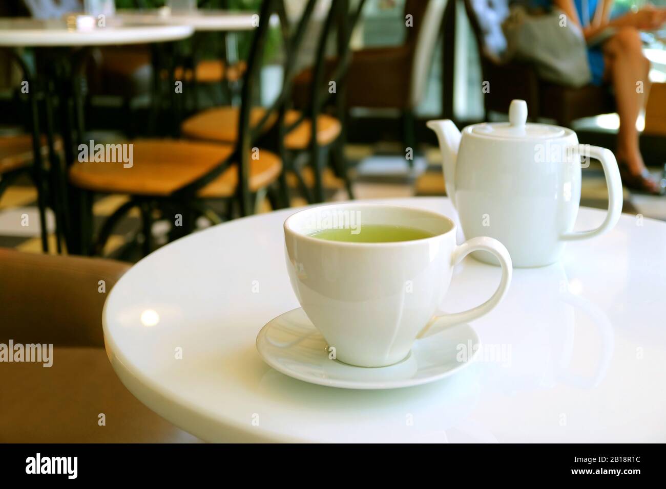 Closeup a cup of green tea and teapot on white round table in a tearoom ...