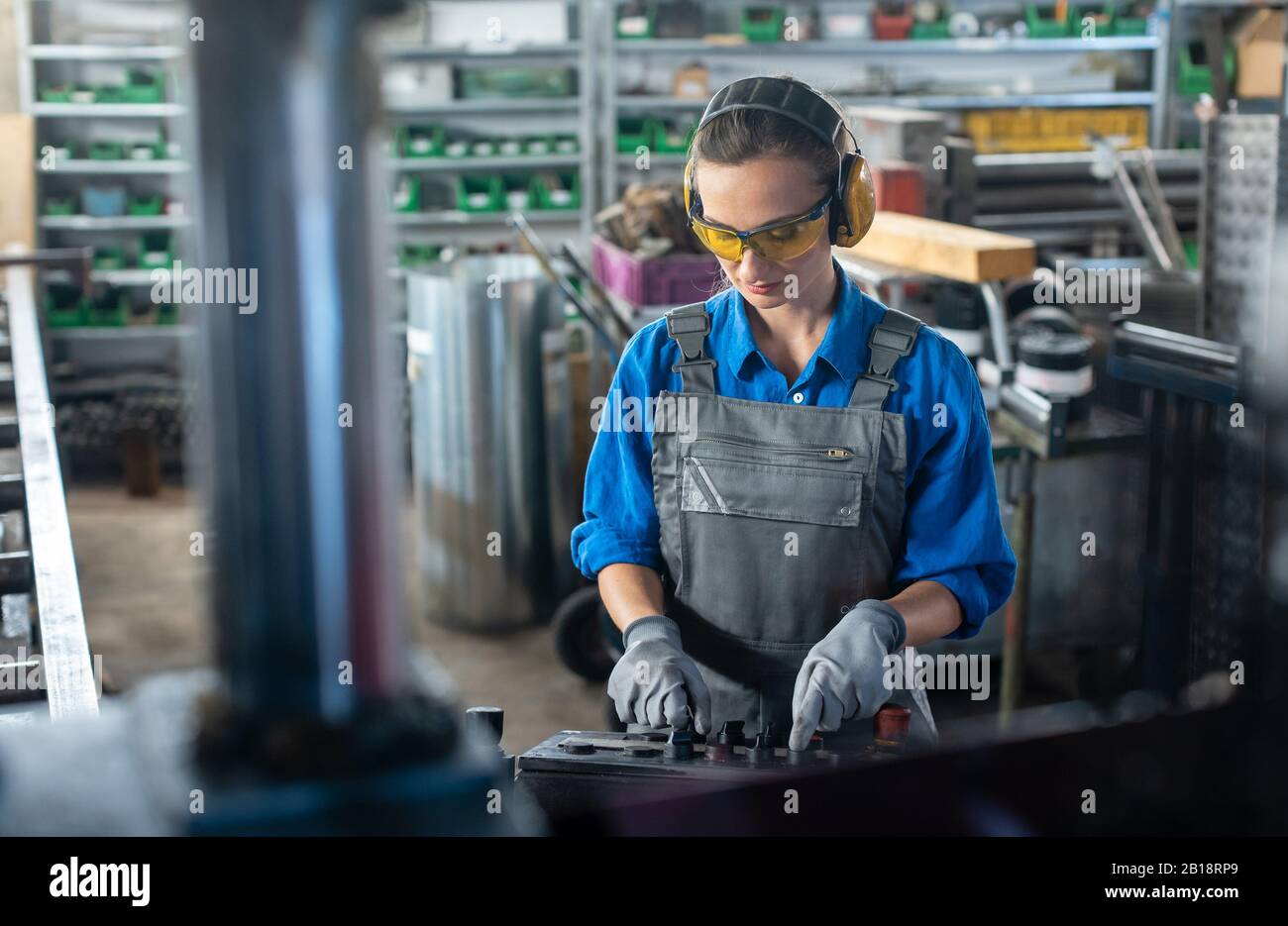 Woman worker operating a machine tool in metal workshop or factory ...