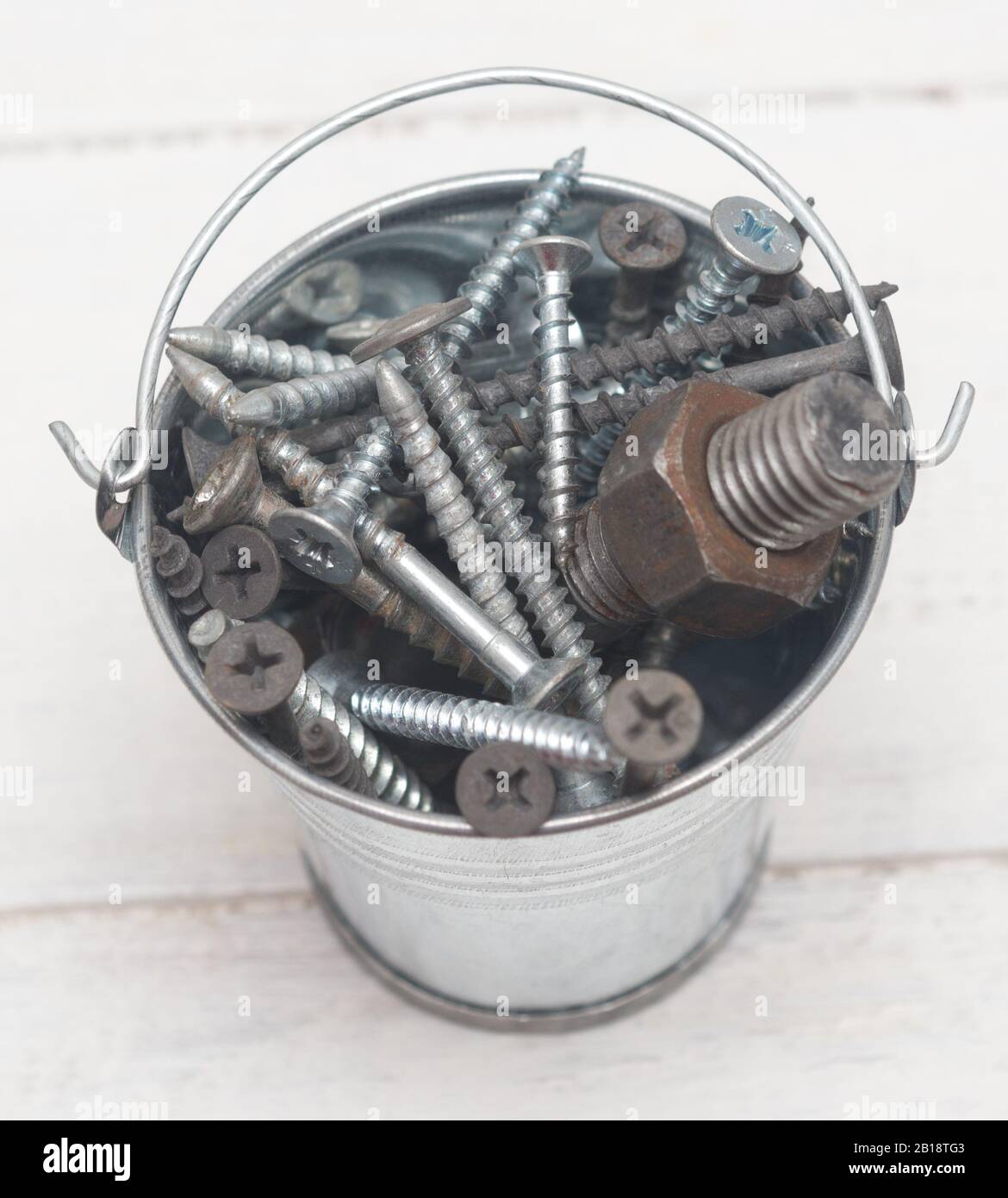 Screws and bolts in a bucket on a wooden background Stock Photo - Alamy