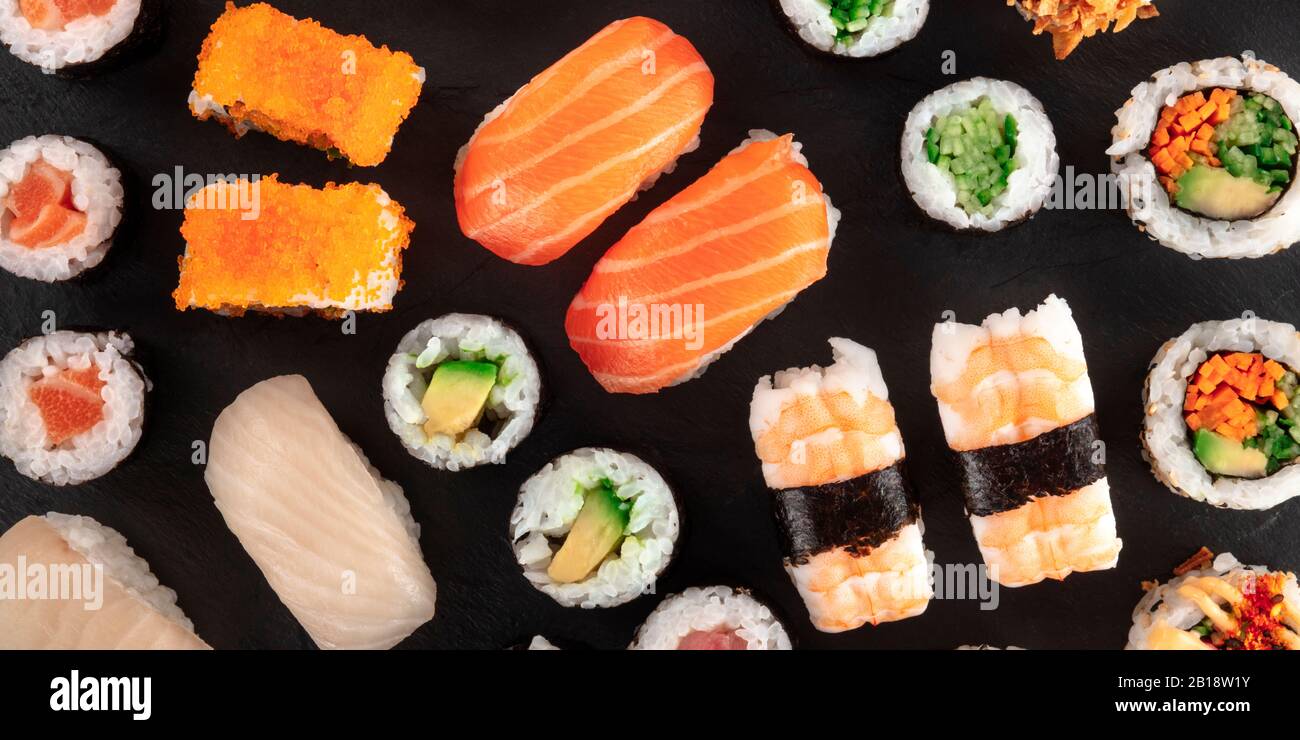 Large sushi set panorama, close-up top shot on a black background. An ...
