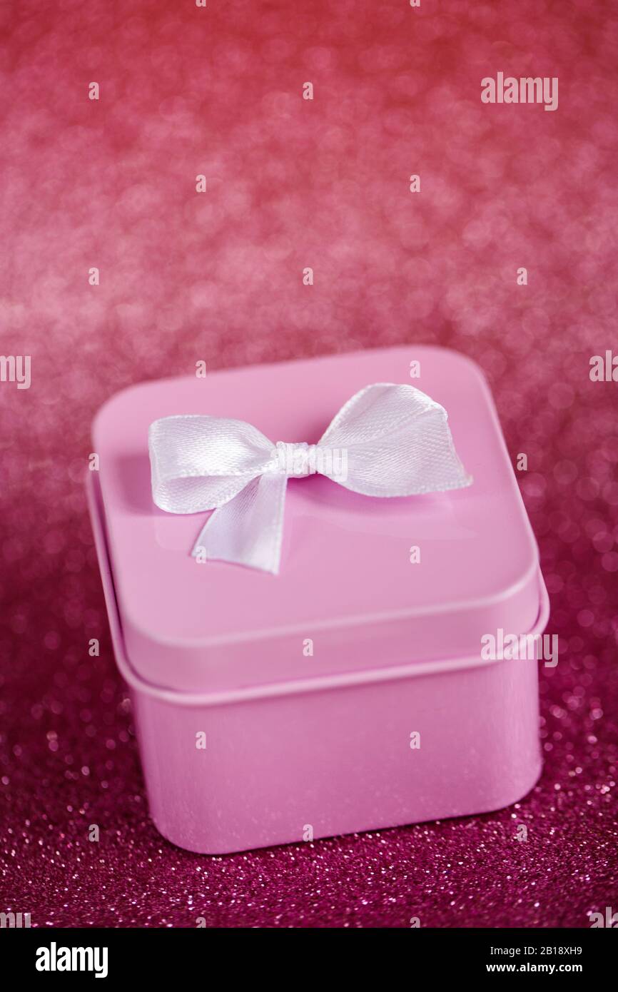Small square metal gift box with white bow on dark pink background with ...