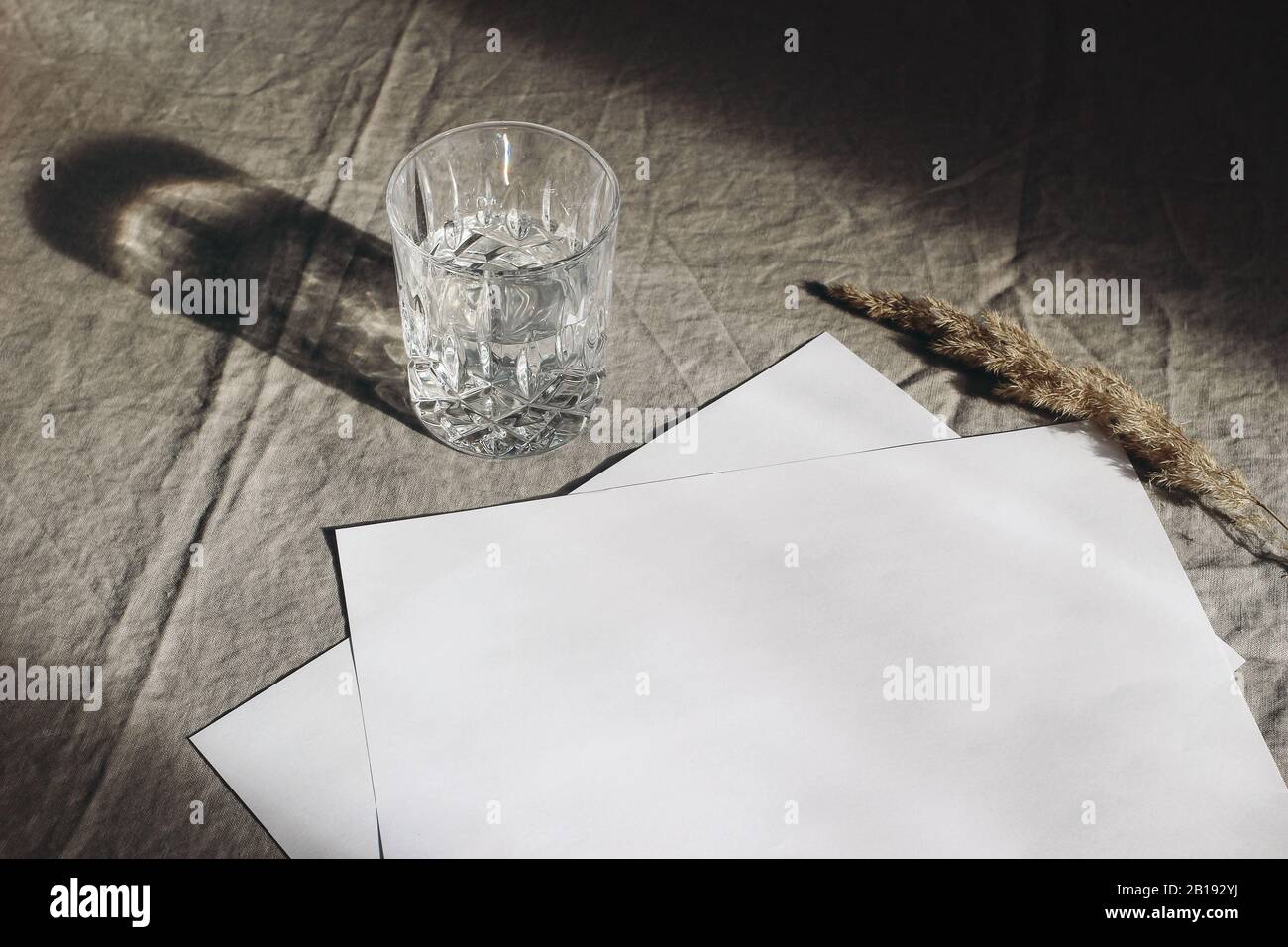 Stationery still life scene. Glass of water, dry grass on beige linen ...