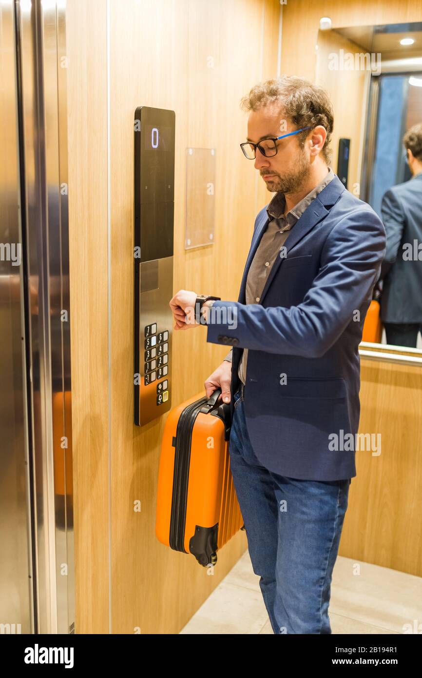 Businessman with luggage looking at smart watch in elevator Stock Photo ...