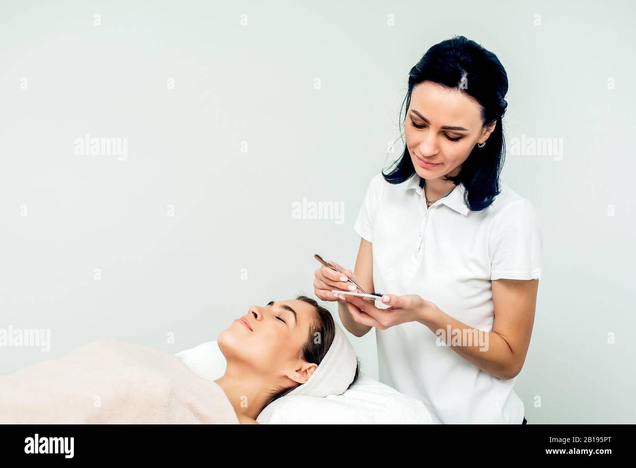 Cosmetologist and patient during eyelash extension procedure on white ...