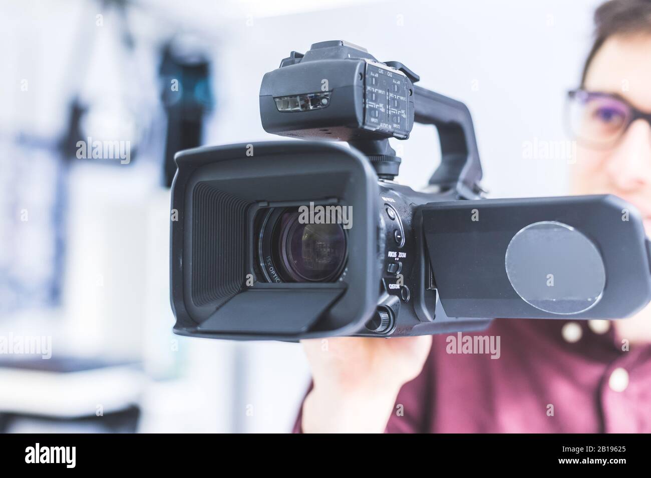 Male cameraman is holding a professional video camcorder, blurry ...