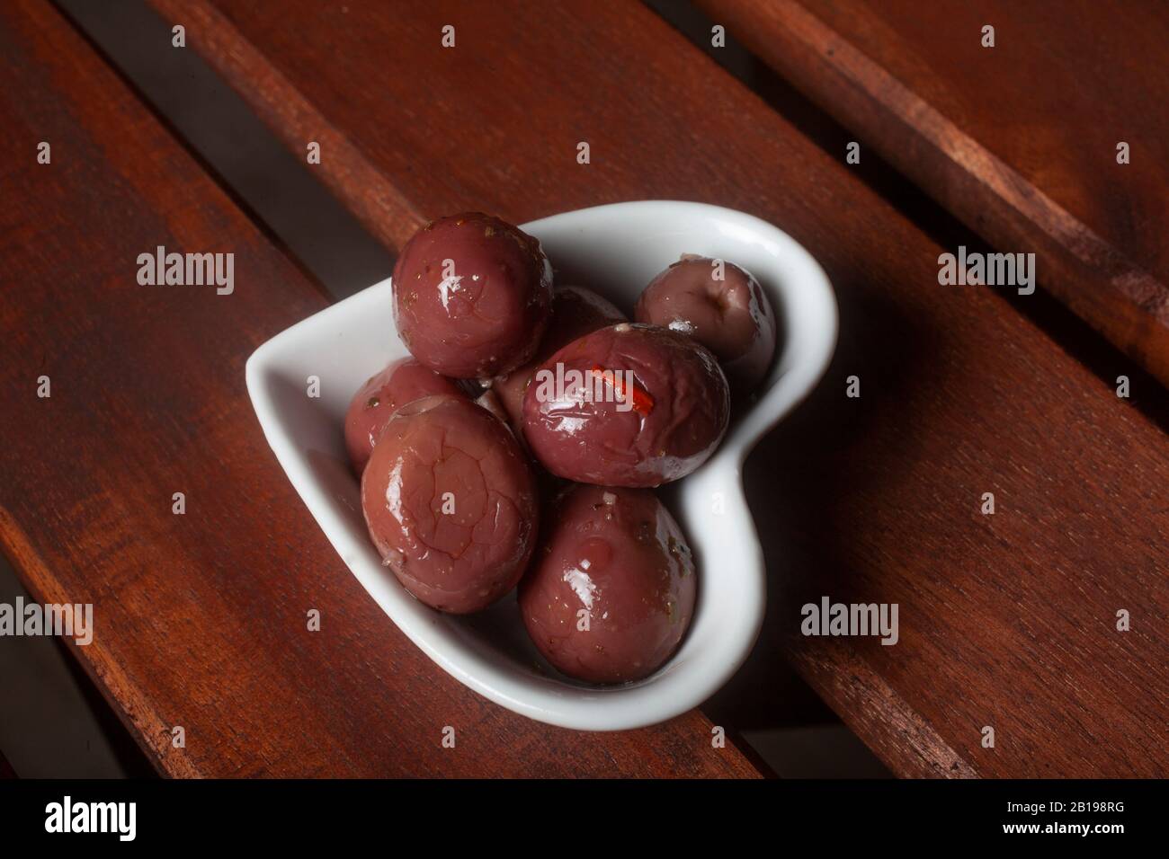 dark olives in spicy brine in a white ceramic heart-shaped bowl on a ...