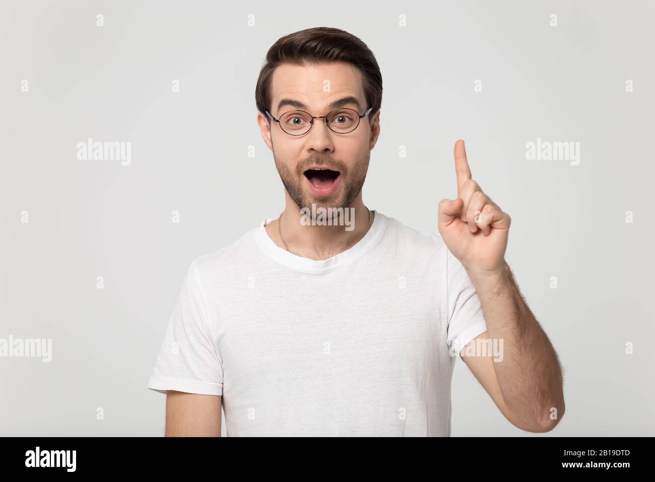 Surprised happy millennial man rising finger up on empty copyspace ...