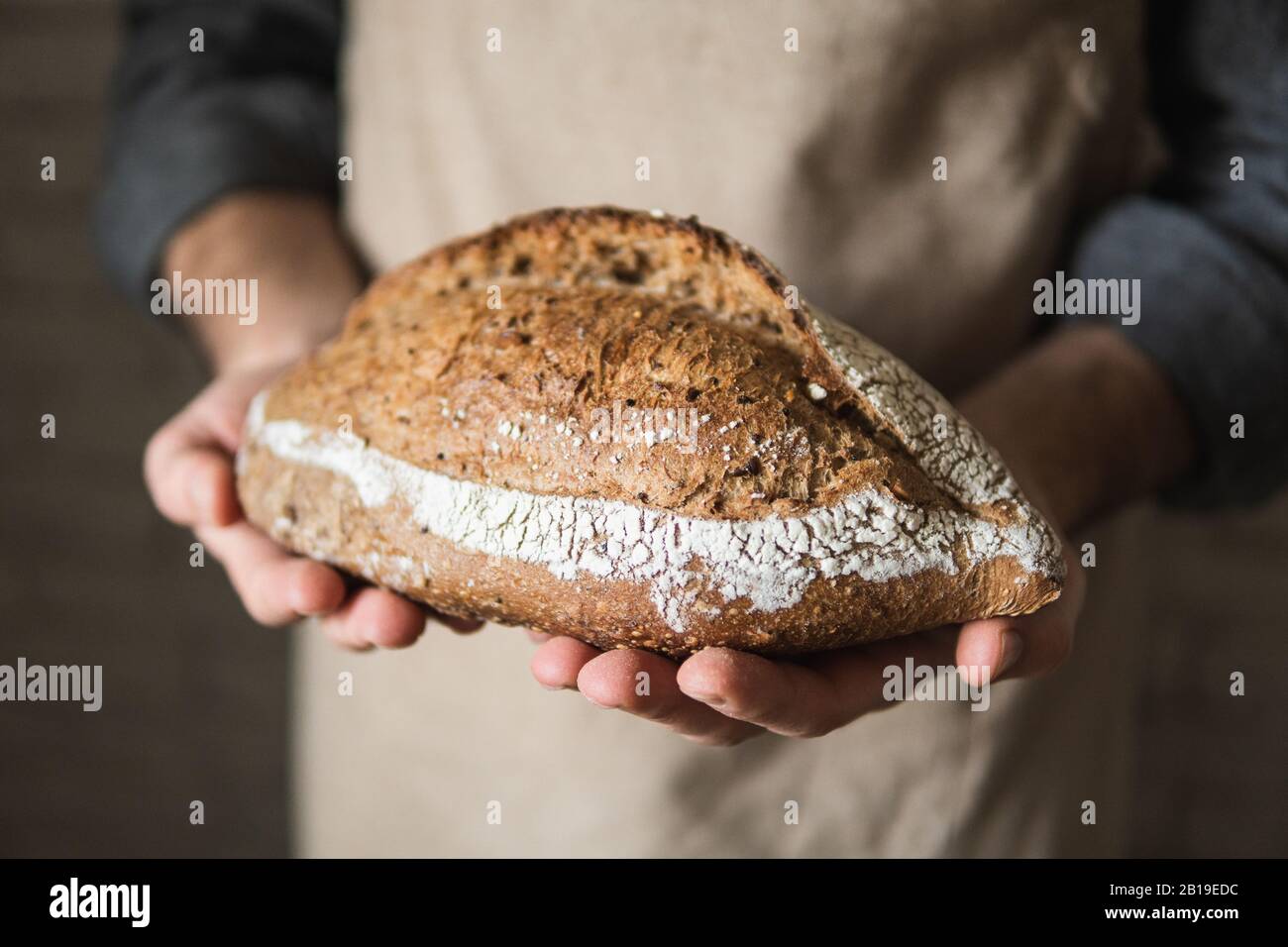 Man in rustic apron holding a loaf of bread in his hands. Close up on ...