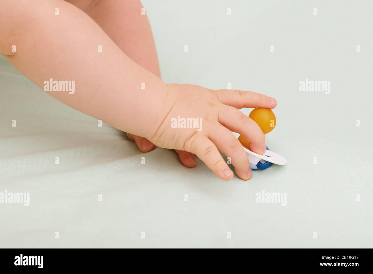 Baby hands holding a pacifier on light green background Stock Photo - Alamy