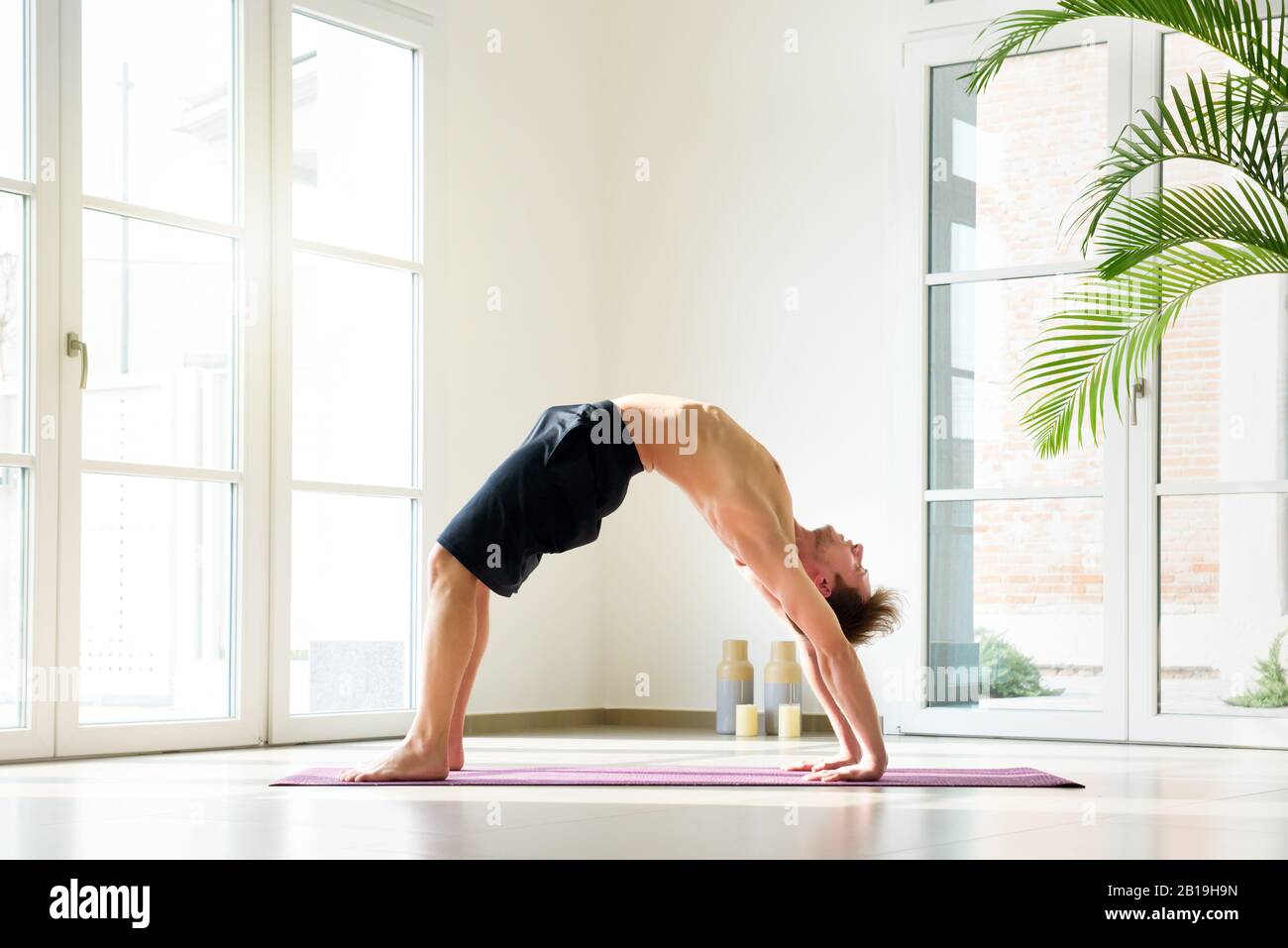 Shirtless young man practicing yoga doing bridge pose, exercising ...