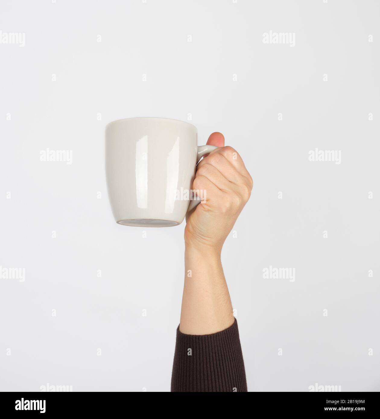white ceramic cup in a female hand on a white background, hand is ...