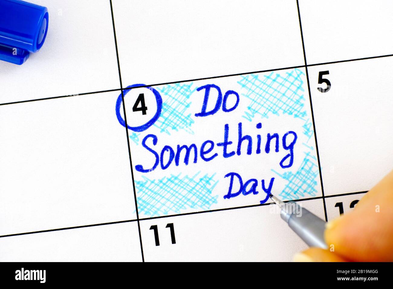 Woman fingers with pen writing reminder Do Something Day in calendar ...