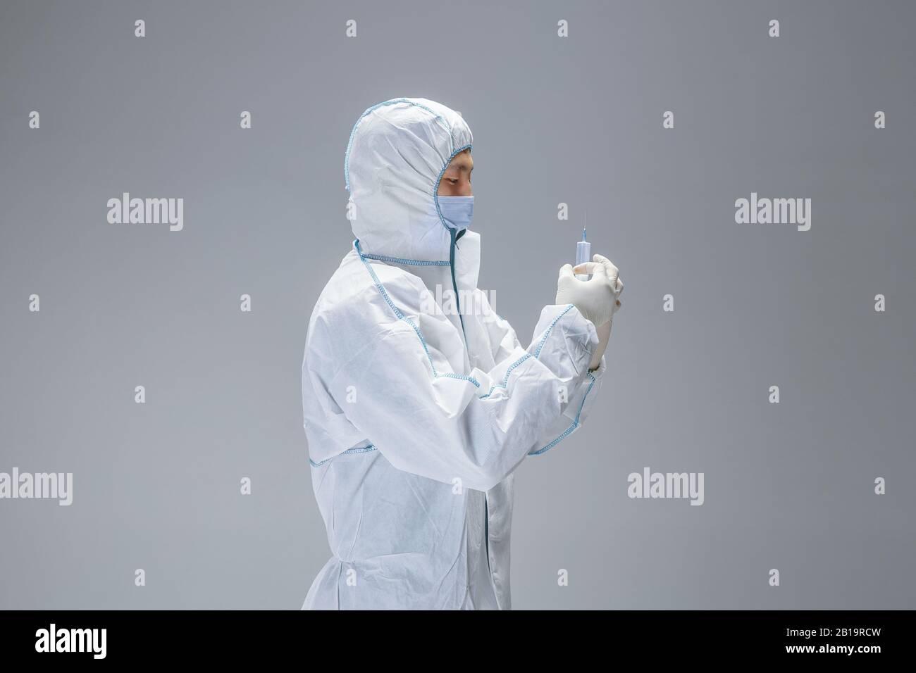 Prevention. Medic in white hazmat protective suit prepares a syringe ...