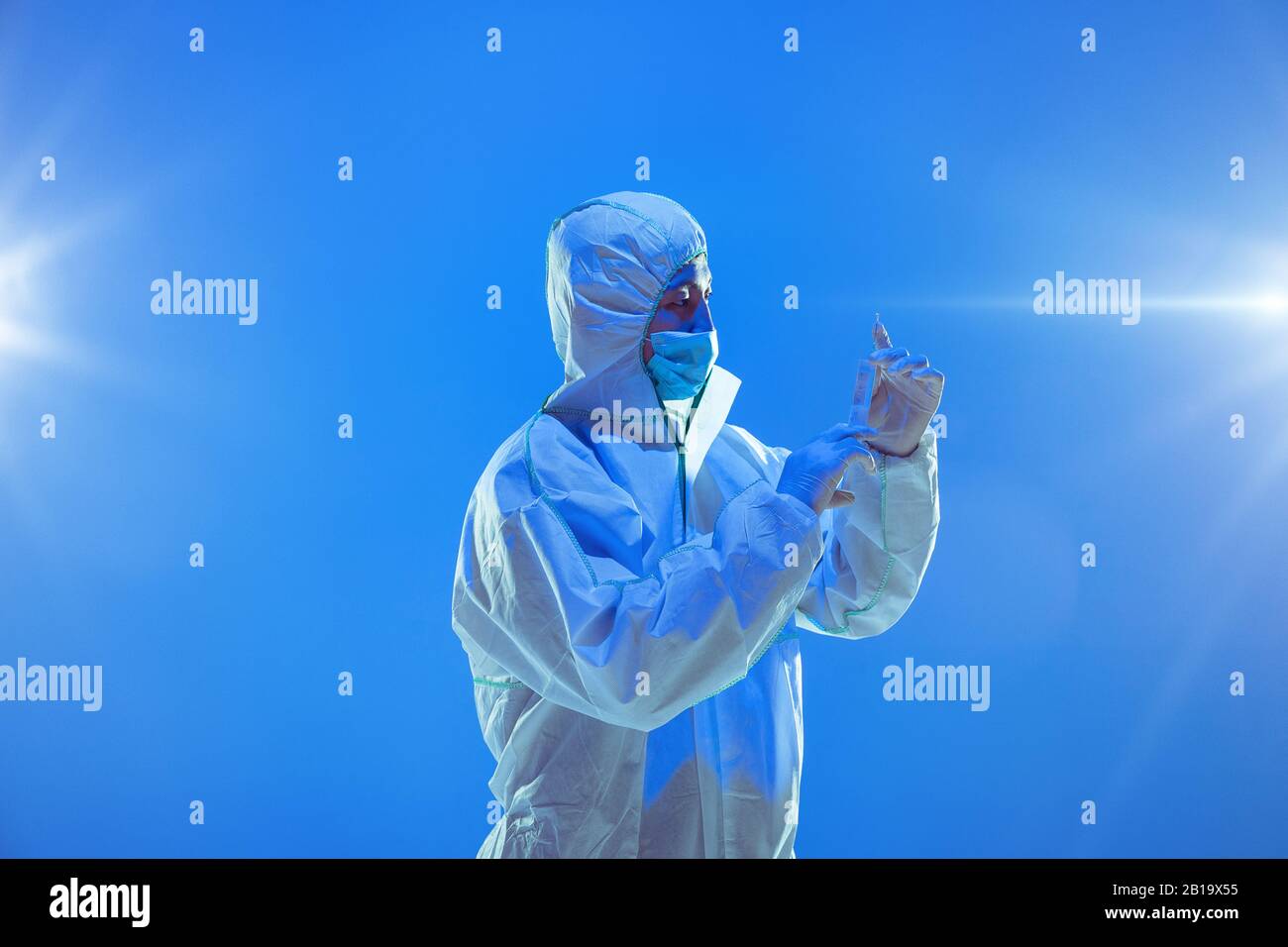 Prevention. Medic in white hazmat protective suit prepares a syringe ...