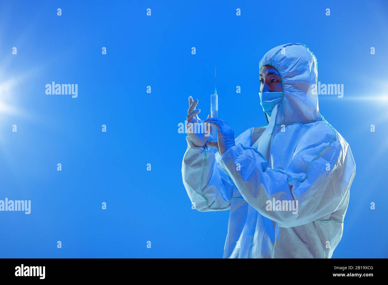 Prevention. Medic in white hazmat protective suit prepares a syringe ...