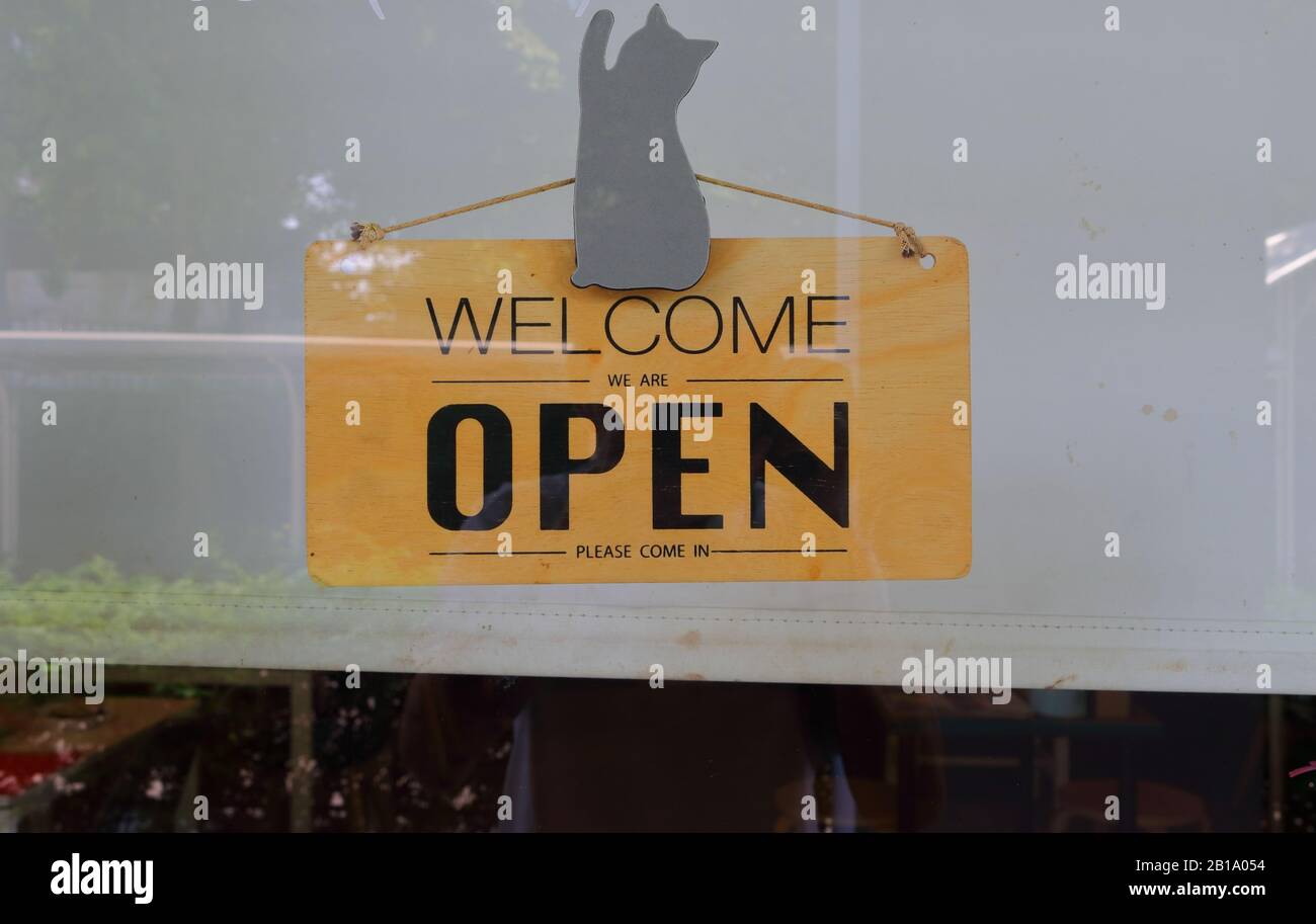 Closeup wooden sign read welcome, we are open, please come in hanging with rope on storefront of ...