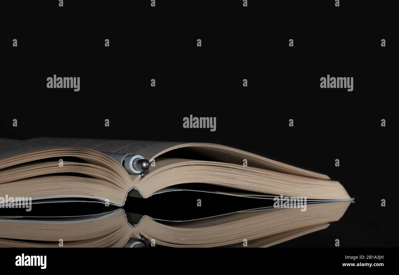 Opened book on black background with mirror reflection and pencil on ...