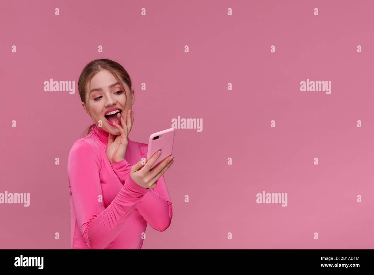 The best day ever. Surpised young redhead woman holding pink smartphone ...