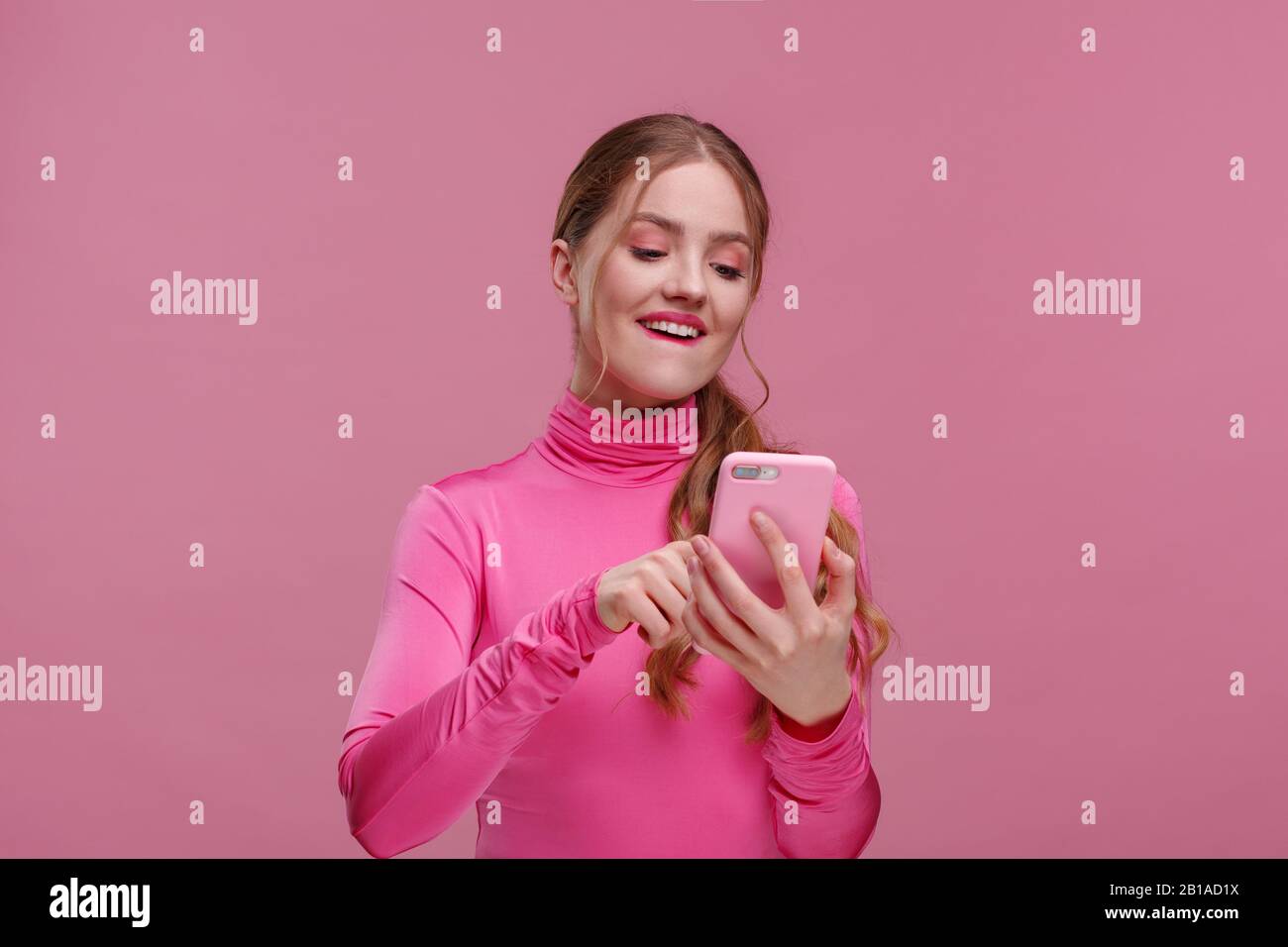 The best day ever. Surpised young redhead woman holding pink smartphone ...