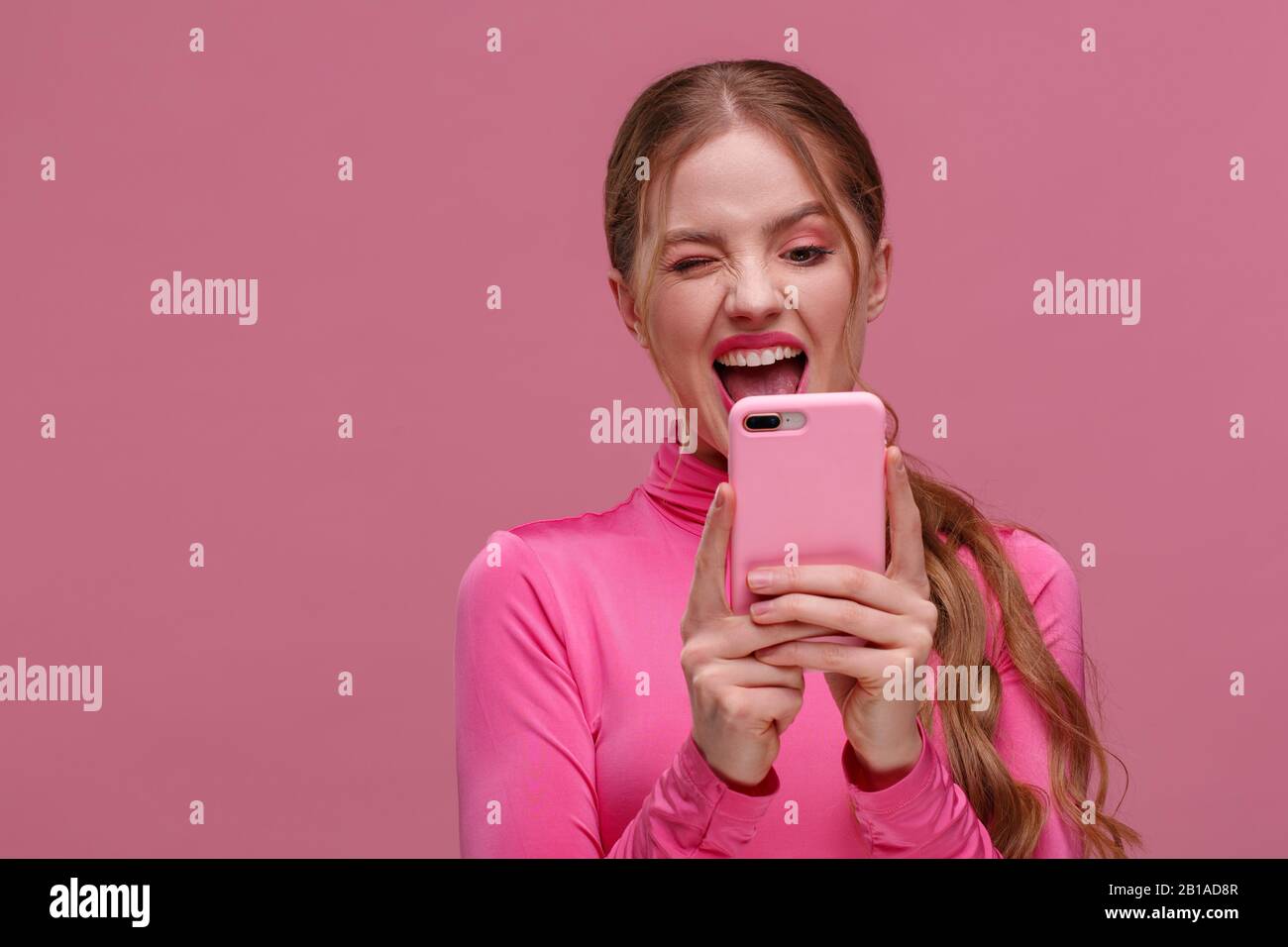 Funny young redhead woman holding pink smartphone and smiling.Happy ...