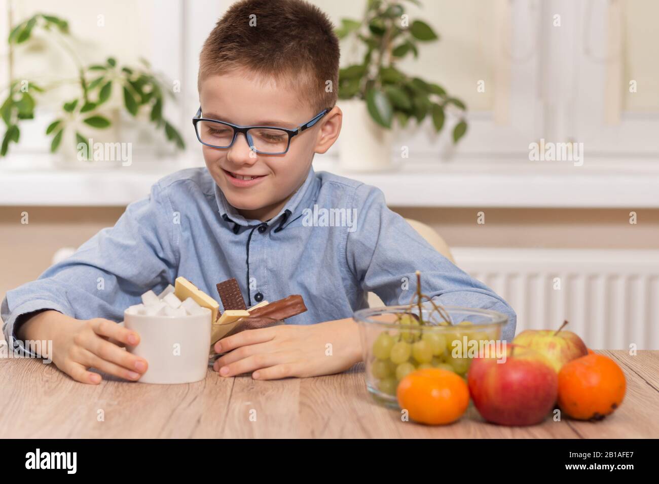 The school-age boy smiles and holds a dish with sweets and a sugar bowl ...