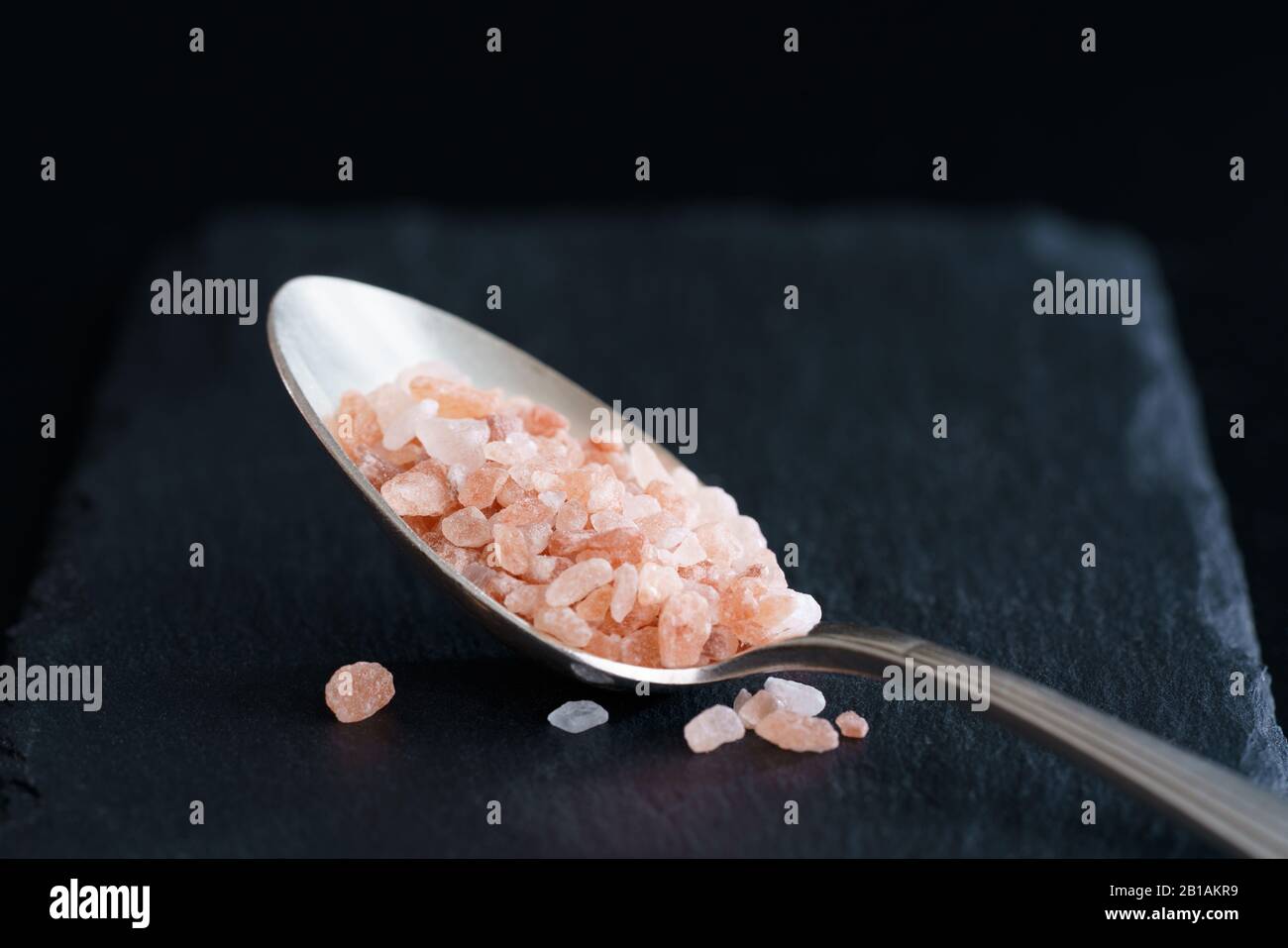 Daily salt intake, 1 teaspoon of pink Himalayan salt. Black background ...
