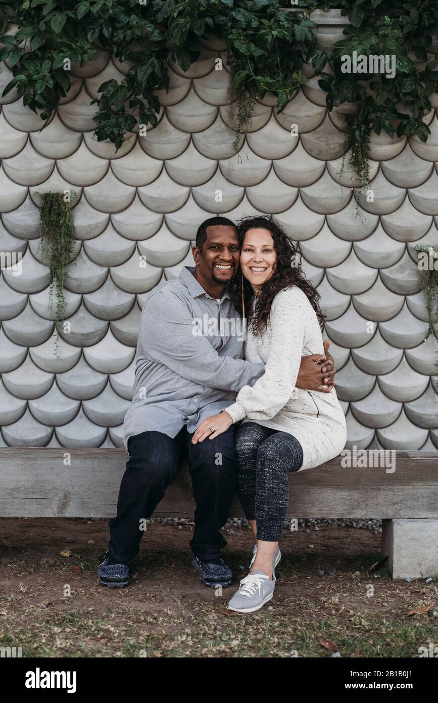 Married couple sitting on park bench smiling and hugging Stock Photo ...