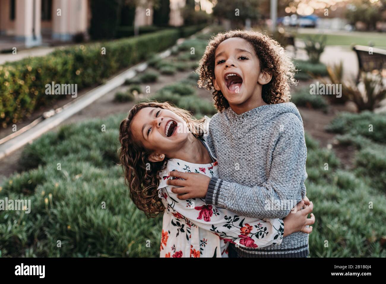 Cute siblings smiling and laughing while hugging outside in sunshine ...