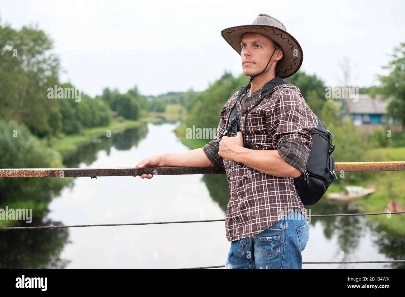 A man in a cowboy hat, with a backpack on the bridge over the river ...