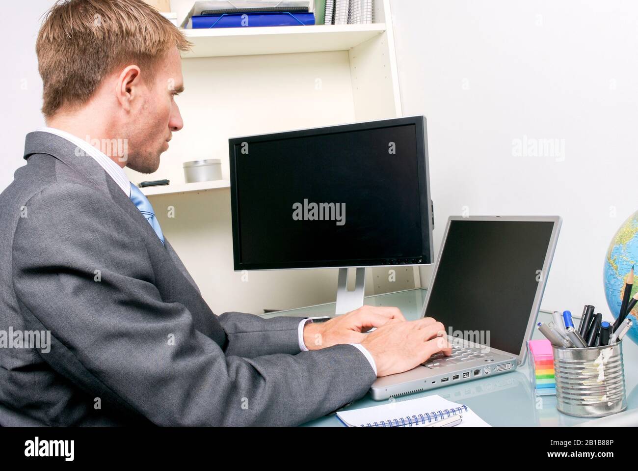 Businessman looking at two computer screens in a small white office ...