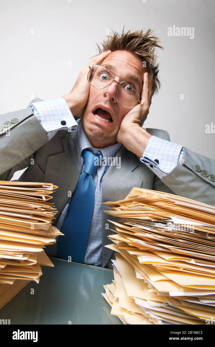 Overwhelmed office worker holding his head in shock at the large piles ...
