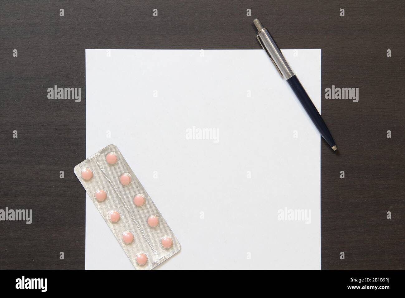 Template of white paper with pen and pills in a blister on dark wenge ...