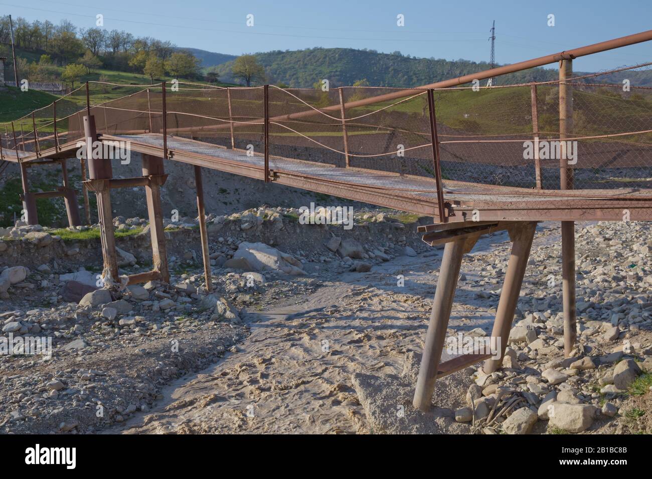 A narrow old rusty river crossing . Dirty, stony river . a suspension ...