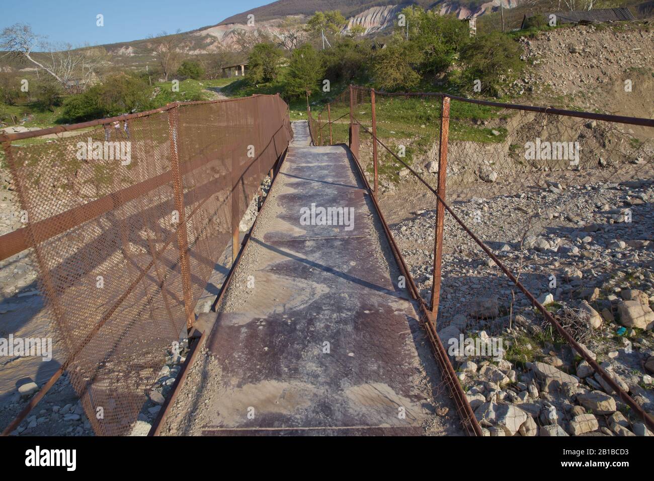 A narrow old rusty river crossing . Dirty, stony river . a suspension ...