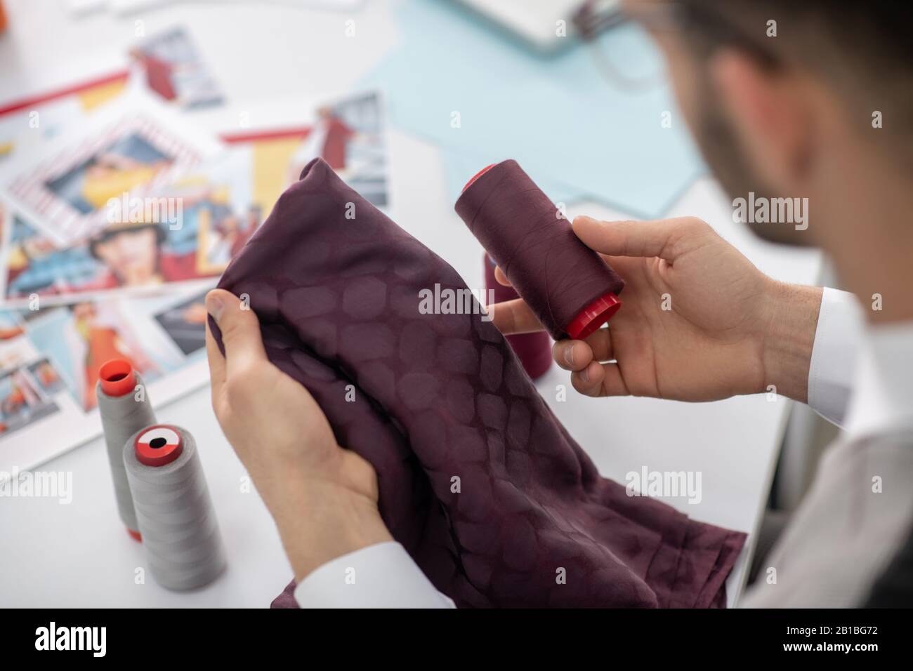 Male tailor holding cloth and spool, matching colors Stock Photo - Alamy