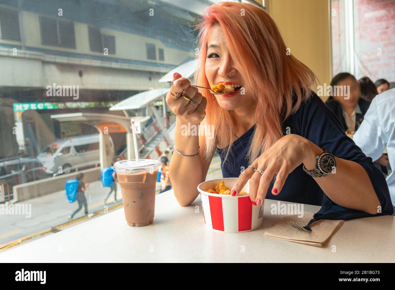 lady eating fried chicken in restaurant beside the road in Bangkok city ...