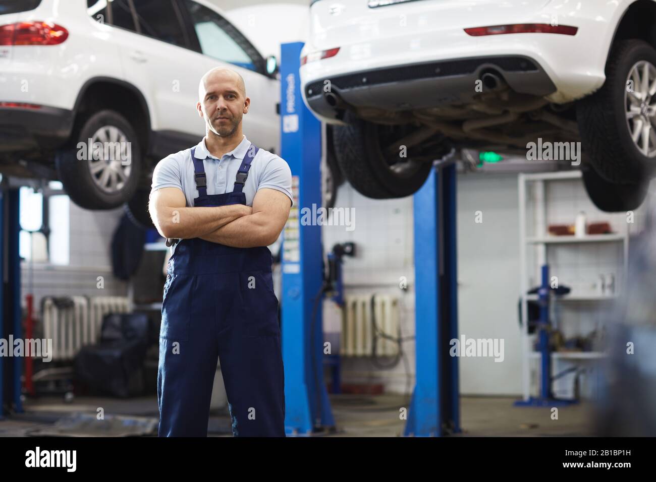 Portrait of muscular car mechanic standing with arms crossed while ...