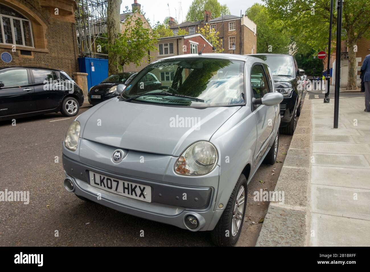 Silver electric Mega City car, parked in the street next to the kerb ...