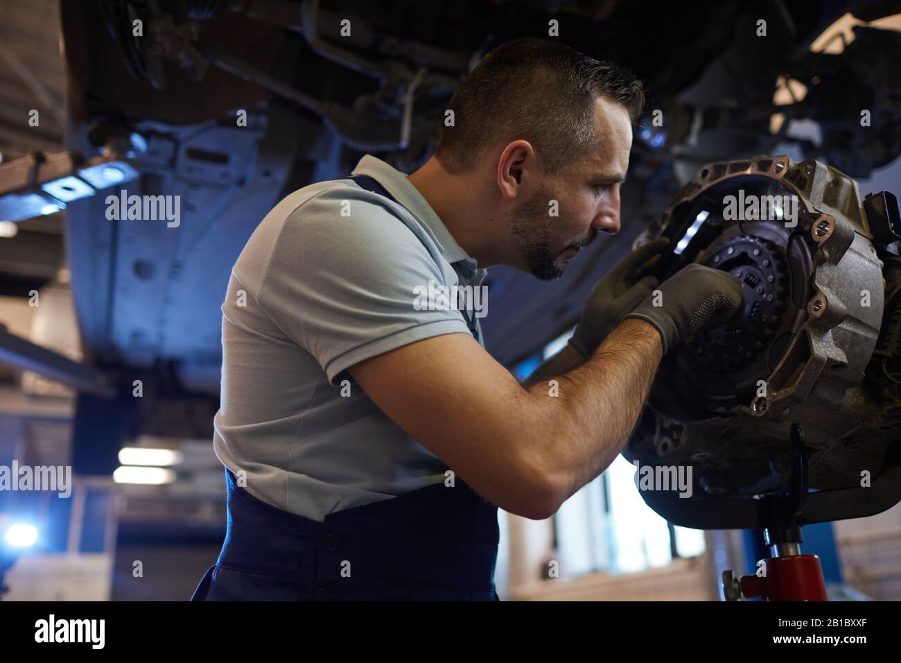 Side view portrait of muscular car mechanic repairing gearbox in auto ...