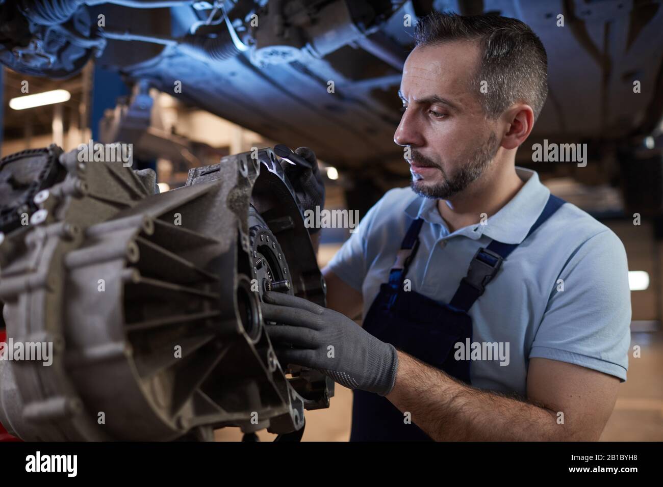 Waist up portrait of muscular car mechanic inspecting car part in auto ...